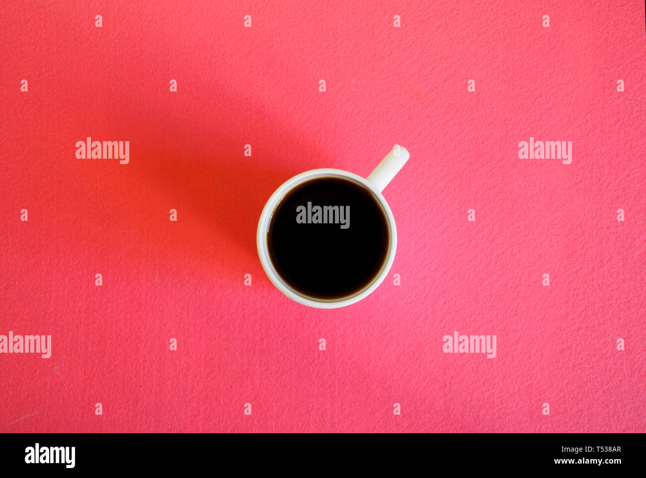 White mug with black coffee on a pink surface. View from above ...