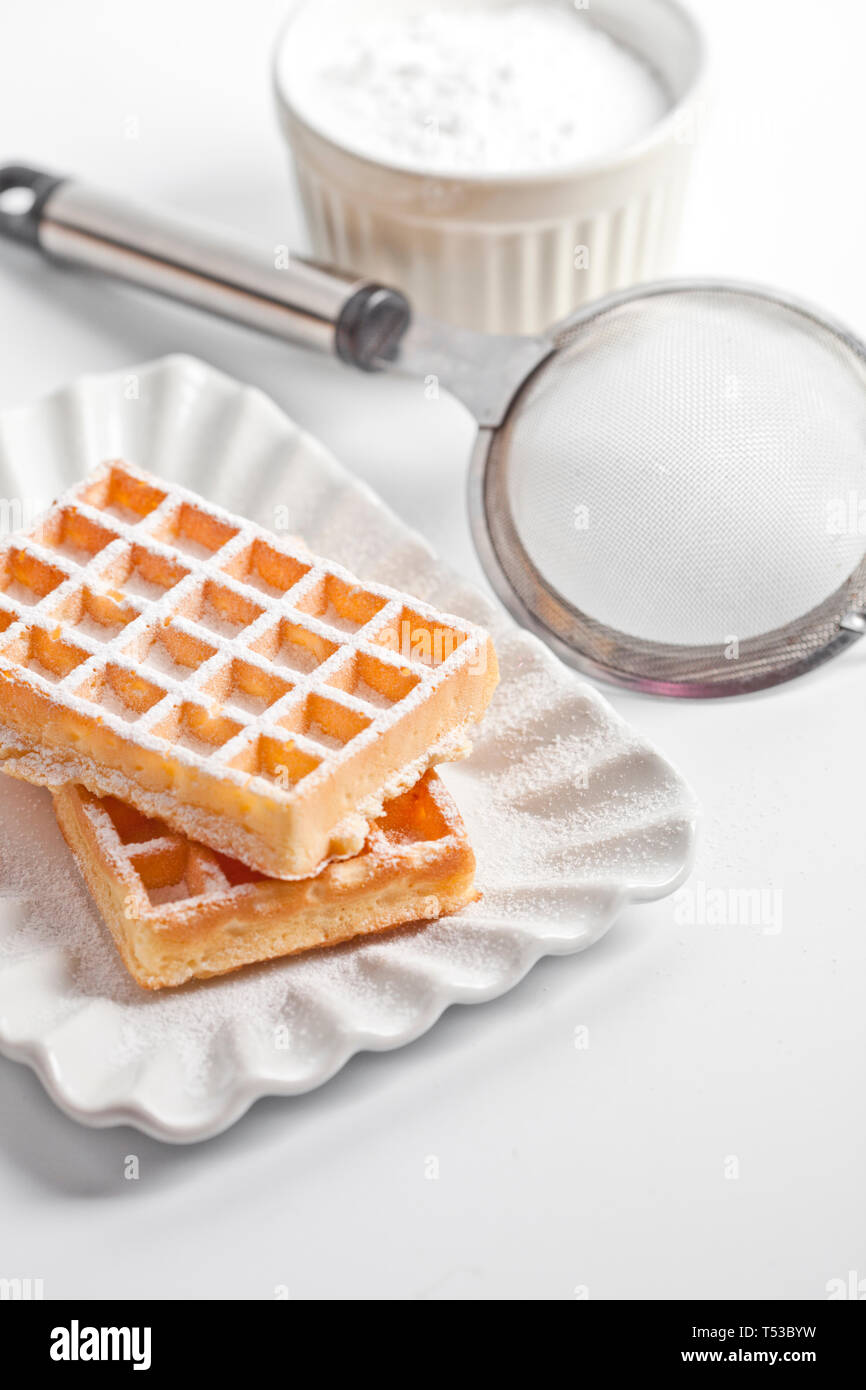 Belgium waffers with sugar powder on ceramic plate and strainer on ...