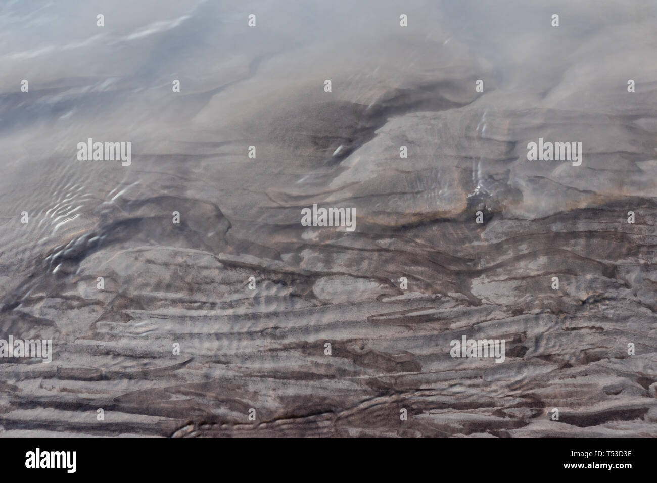 Glacial riverbank shore with wet black silt sand mud water channels ...