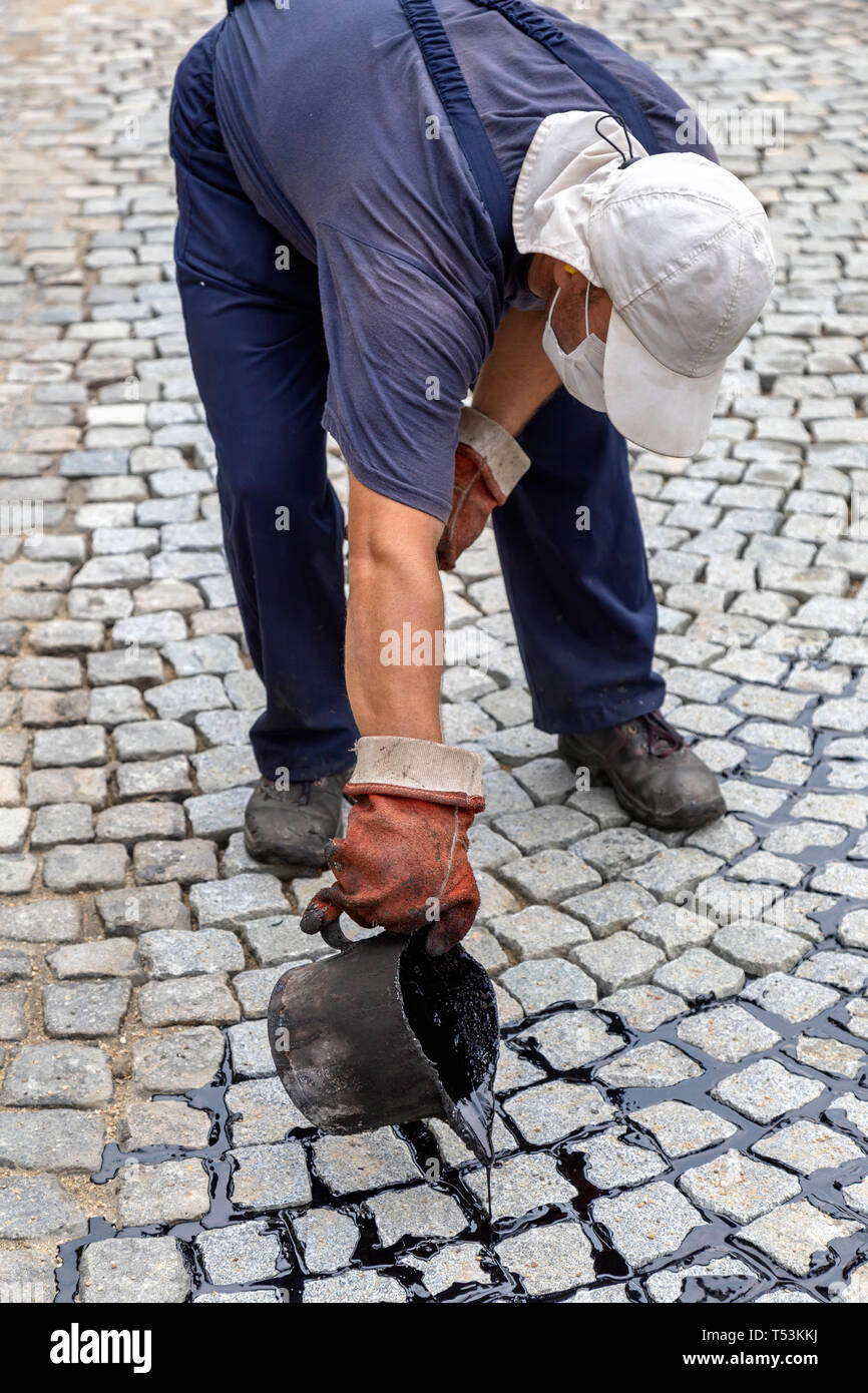 Asphalt worker pouring molten pitch from a tar bucket. Traditional ...