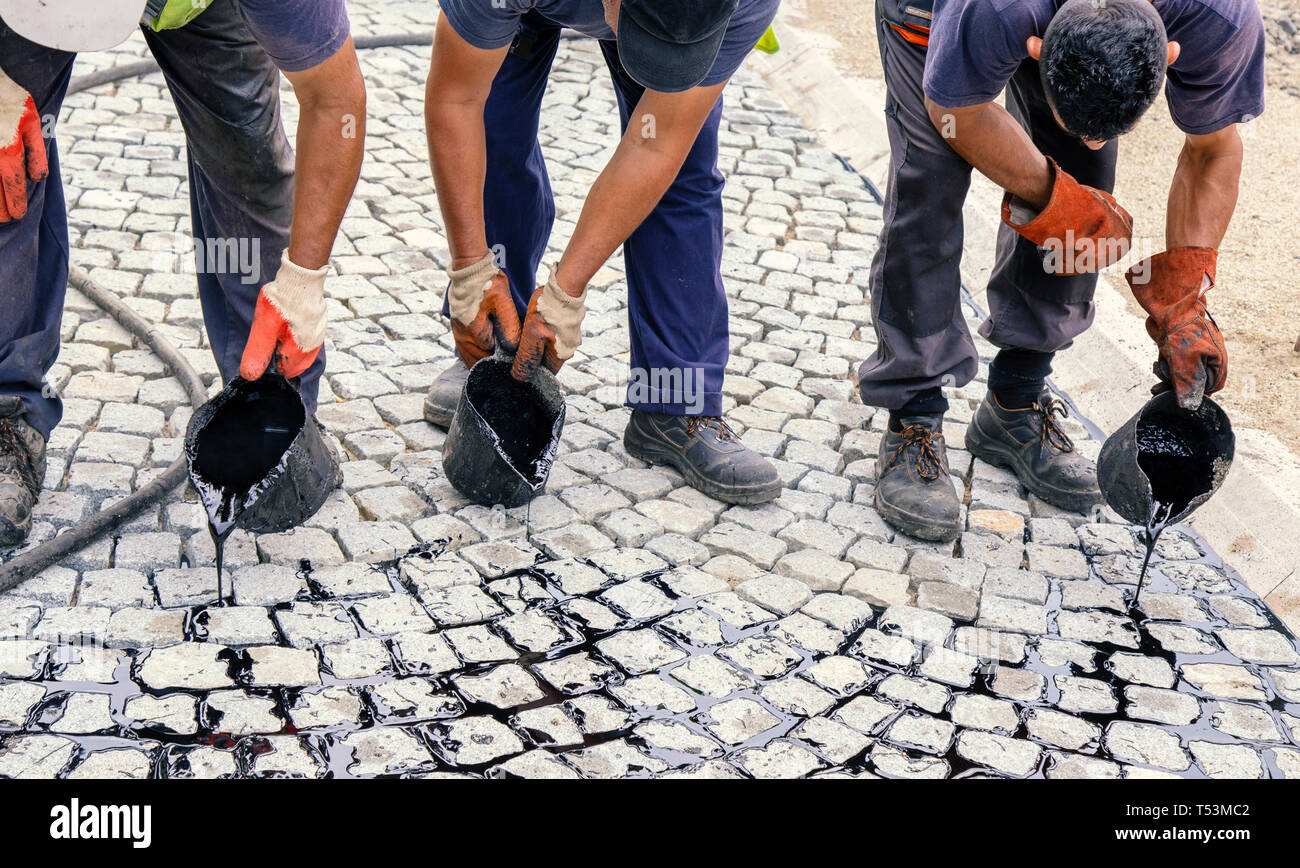 Teamwork on pouring bitumen or thick tar into the joints. Traditional ...