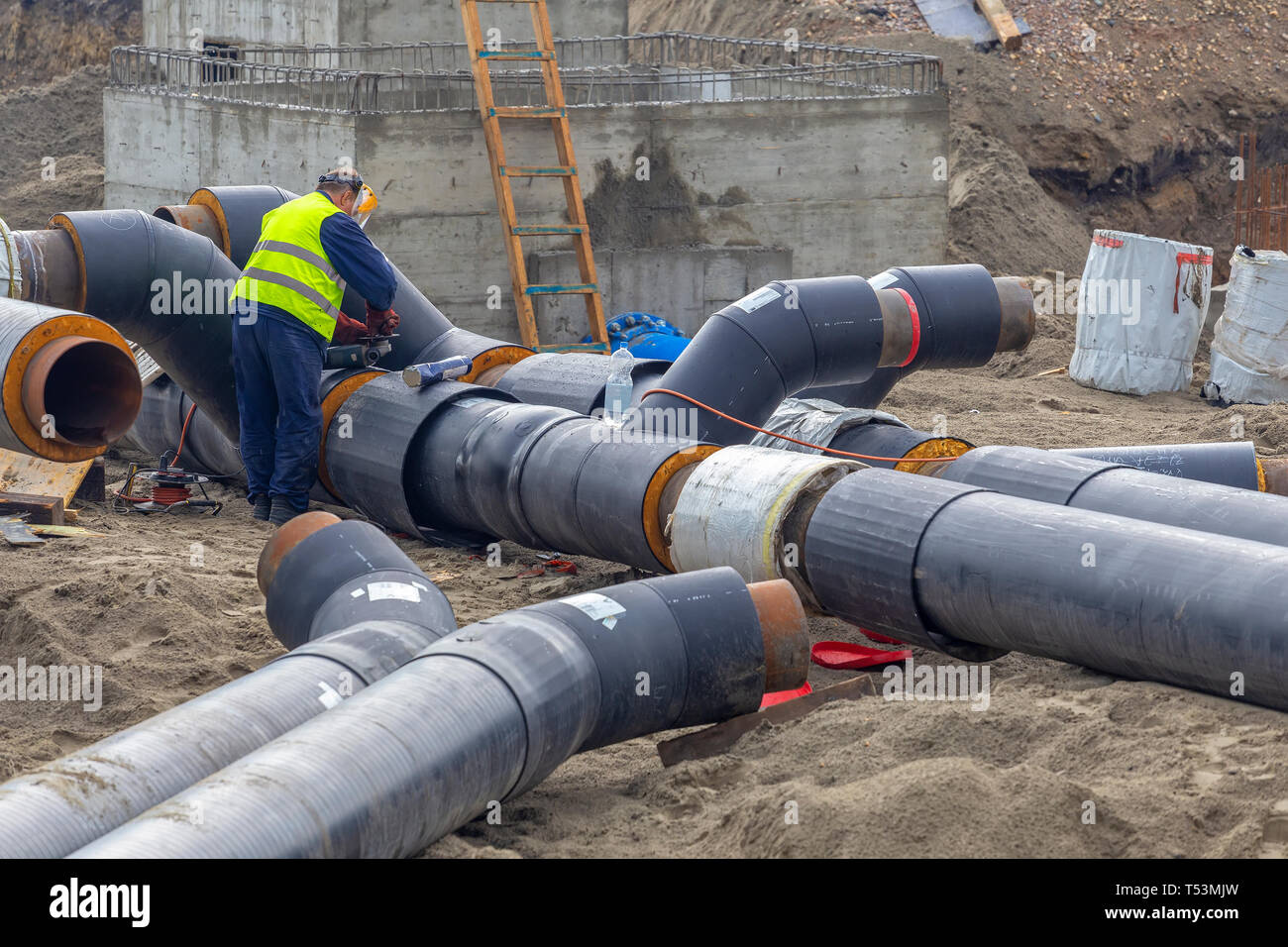 Worker grinding steel pipe, using grinder to work on new pipeline ...