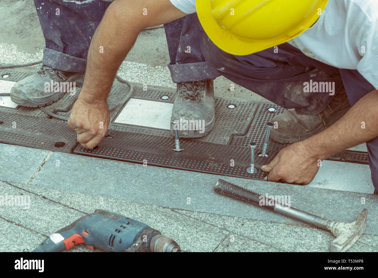 Workers hand screws a screw in a rubber board with a impact wrench ...