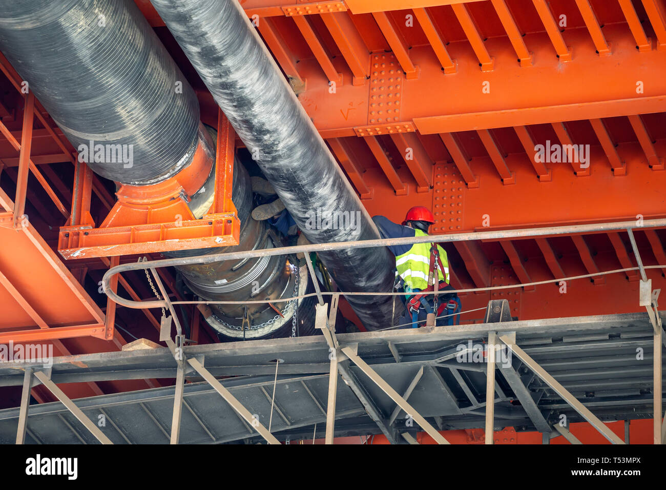 Workers welding district heating pipeline system under metal bridge ...