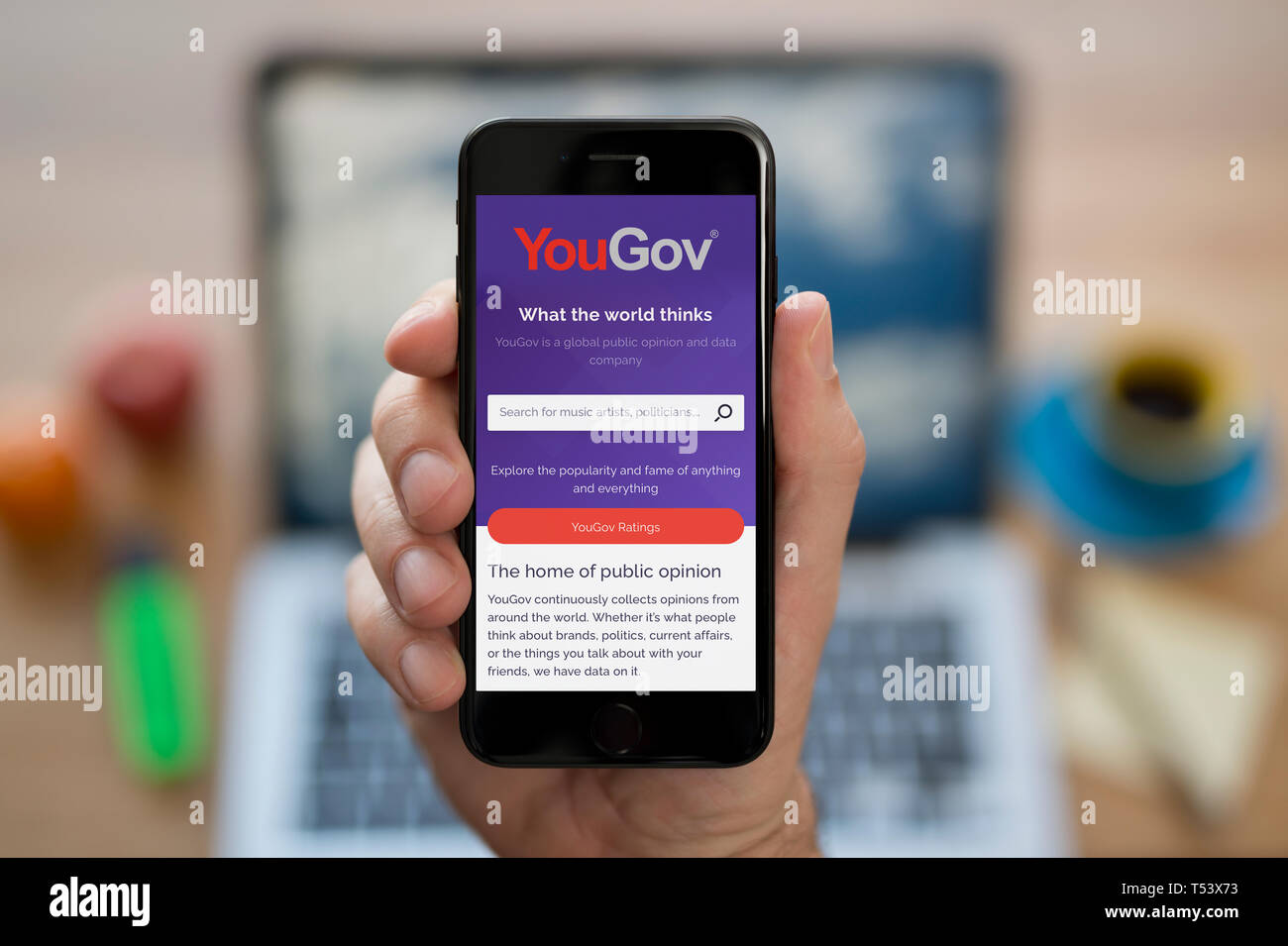 A man looks at his iPhone which displays the YouGov logo (Editorial use ...