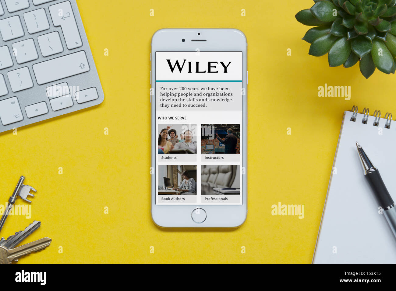 An iPhone showing the Wiley website rests on a yellow background table ...