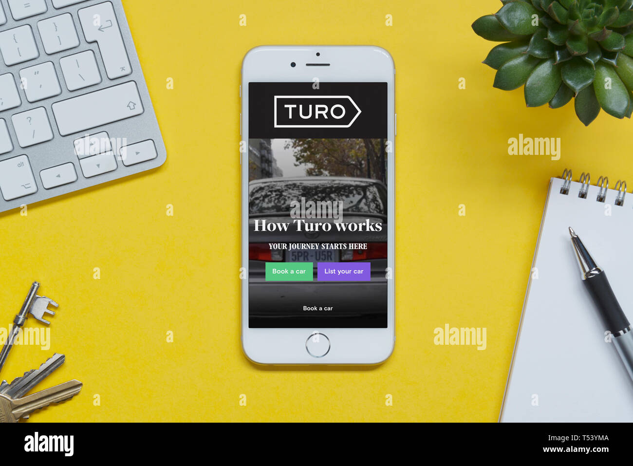 An iPhone showing the Turo website rests on a yellow background table ...
