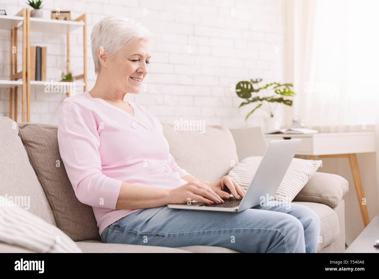 Mature woman typing on her laptop computer, sitting at home, free space ...