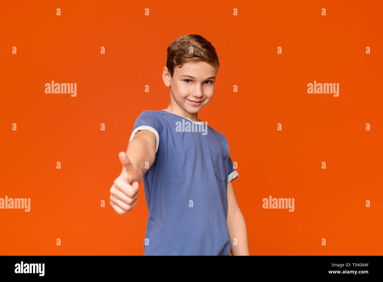Like sign. Cute teen boy showing thumb up gesture, orange studio ...