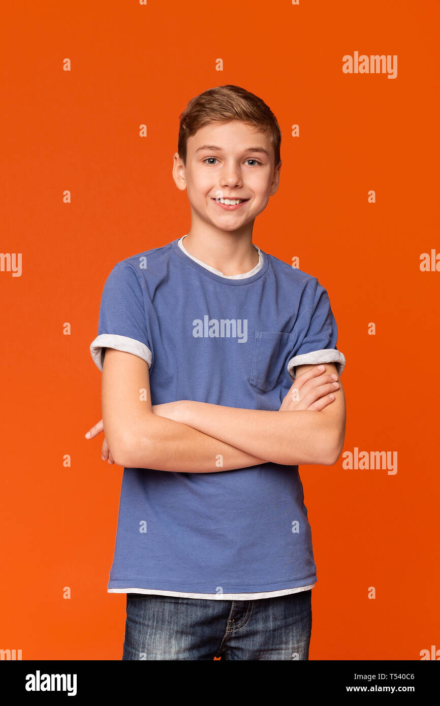 Confident teenager posing with hands folded on orange studio background ...
