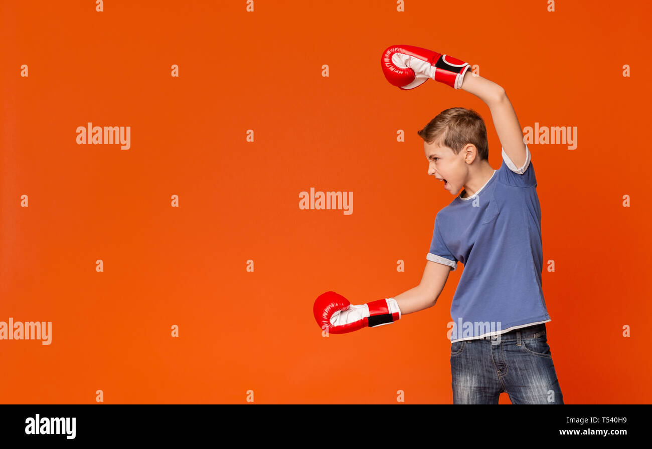Aggressive boy punching in boxing gloves and screaming aside at empty ...