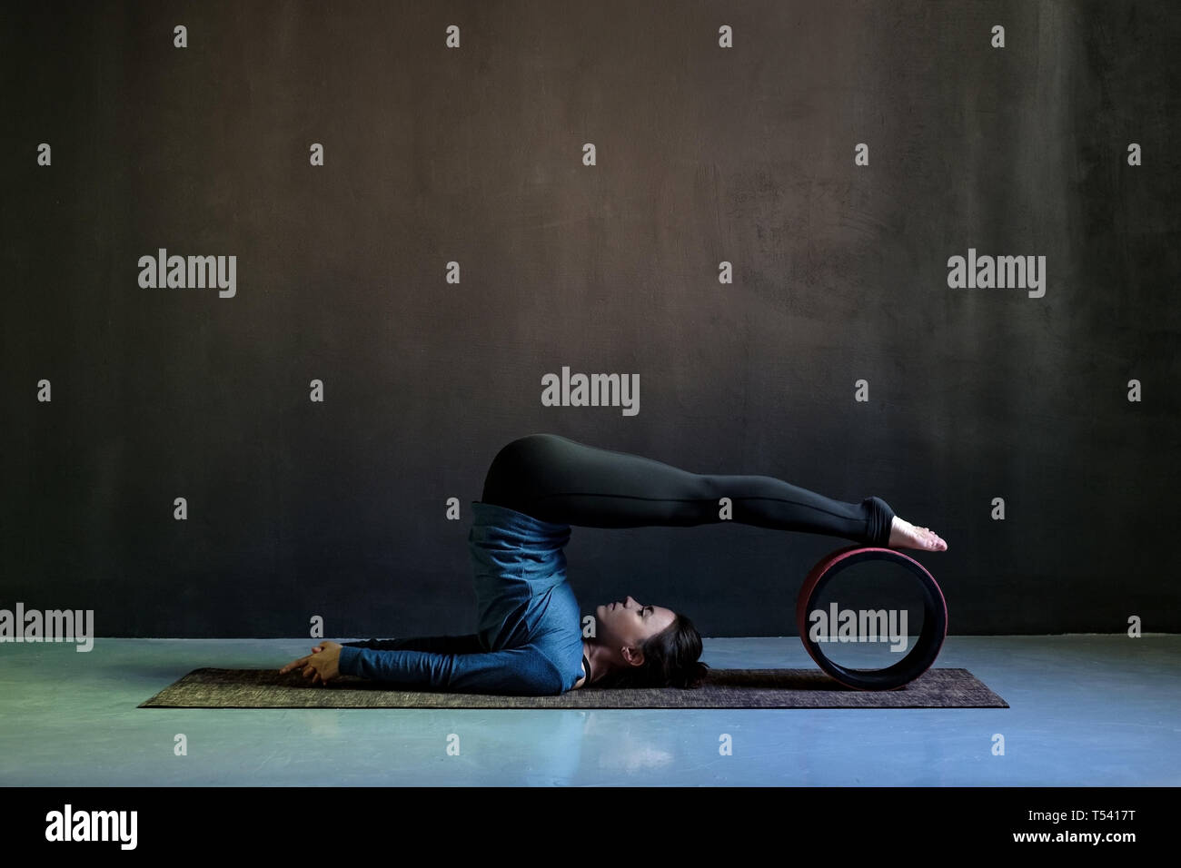 Girl in halasana pose doing yoga on black background Stock Photo - Alamy