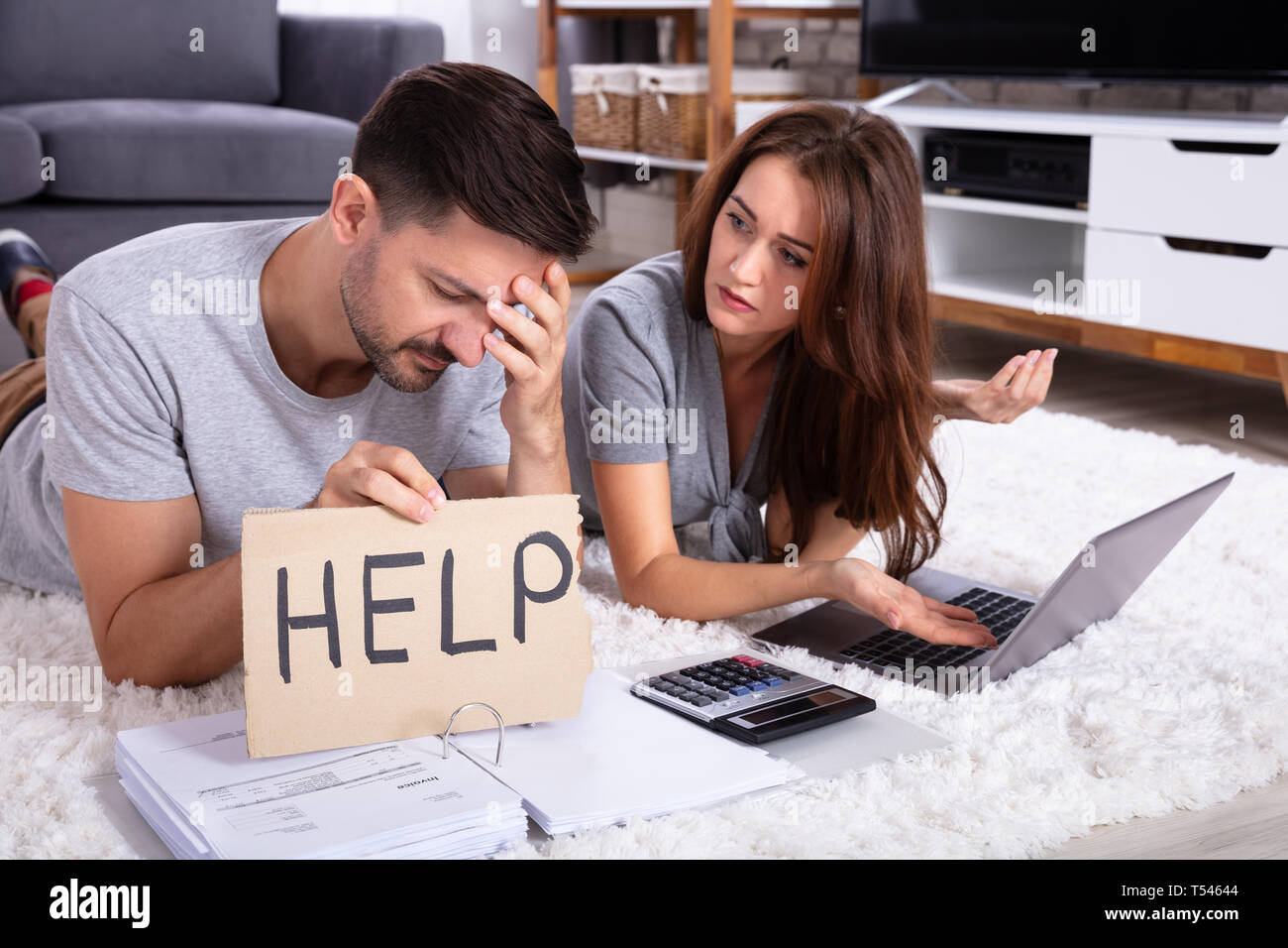 Sad Young Couple Lying On Carpet Holding Help Sign While Calculating ...