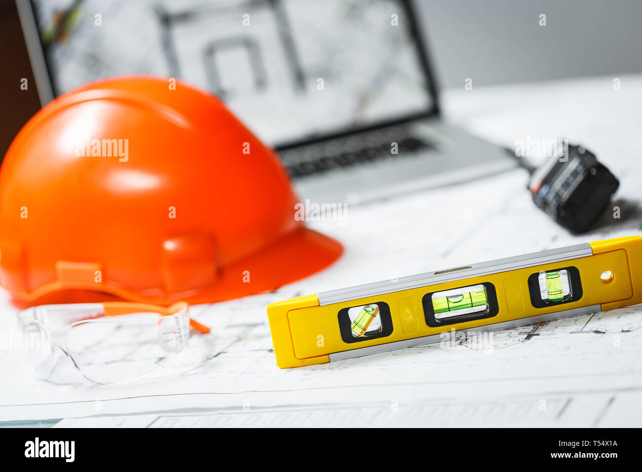 Level meter with blurred Orange hard hat, laptop with drawings and ...