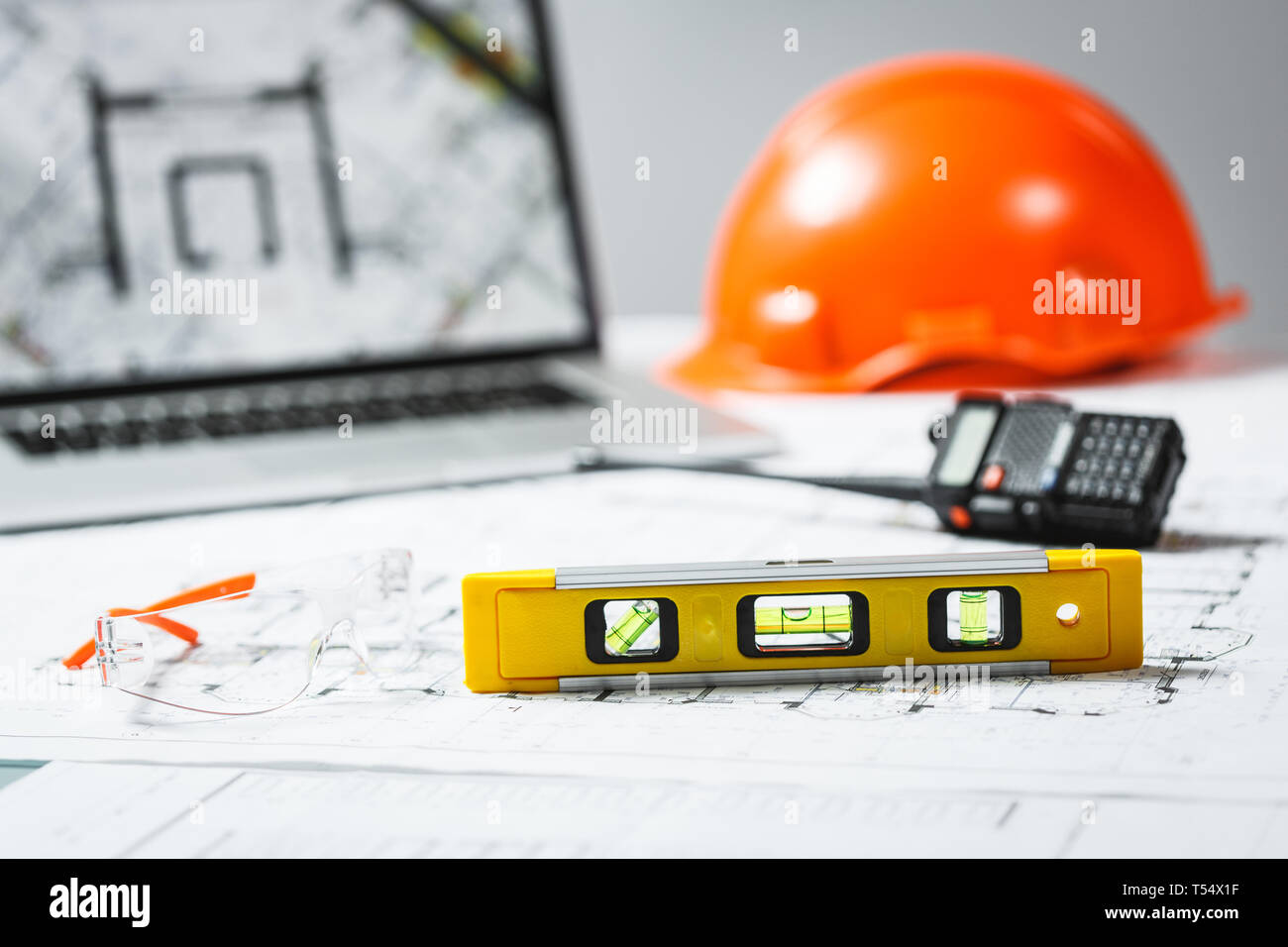 Level meter with blurred Orange hard hat, laptop with drawings and ...