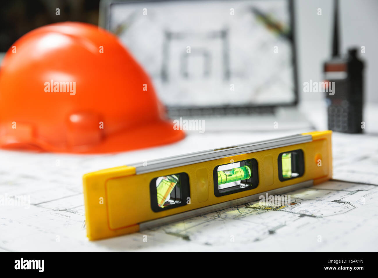 Level meter with blurred Orange hard hat, laptop with drawings and ...