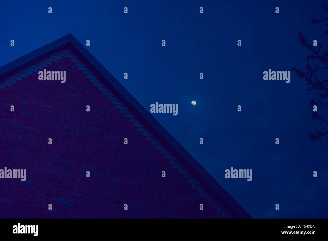 Dark blue sky with a large moon over the roof of the house and the ...
