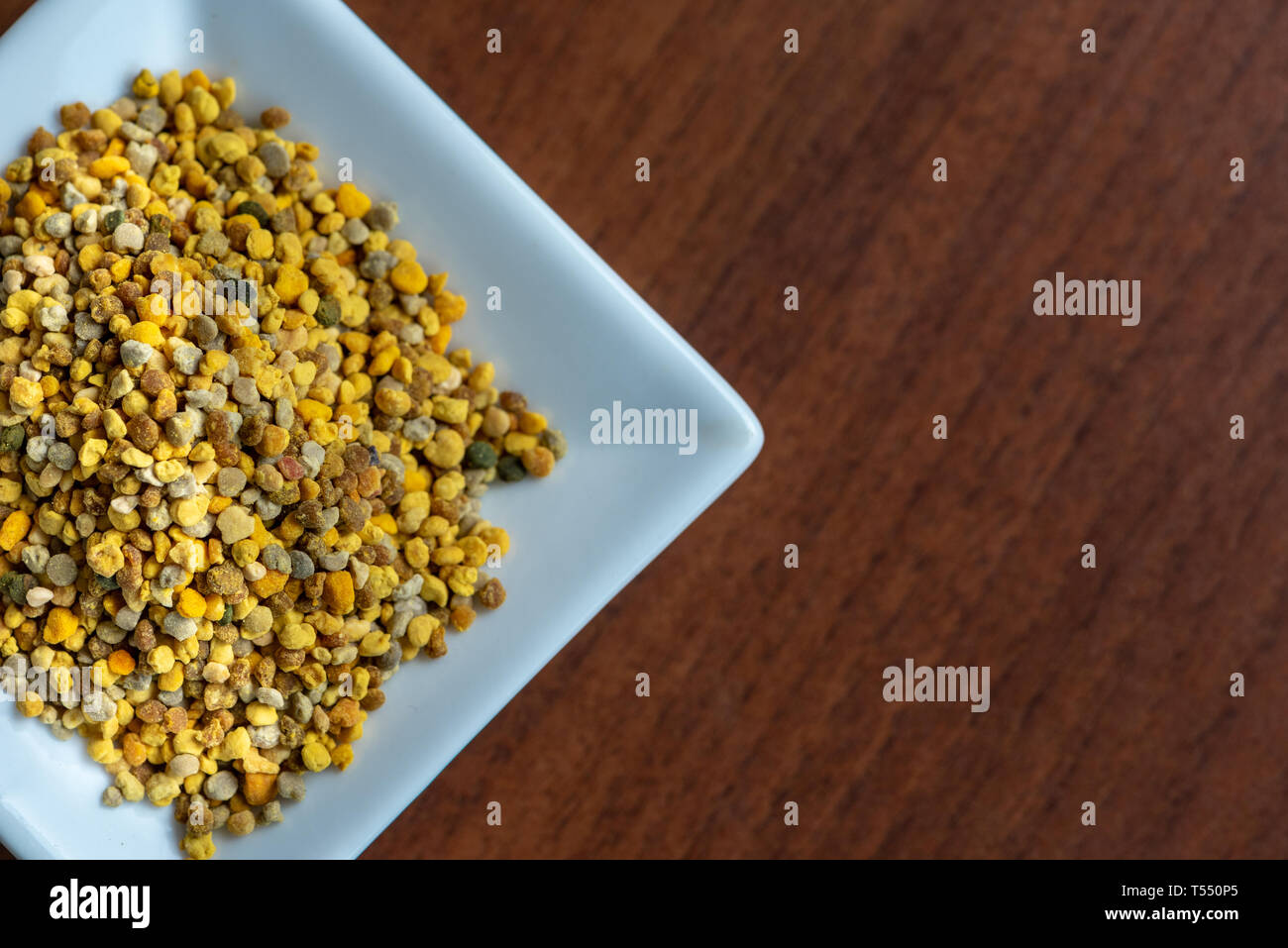 square saucer full of bee pollen on a dark wooden table, view from ...