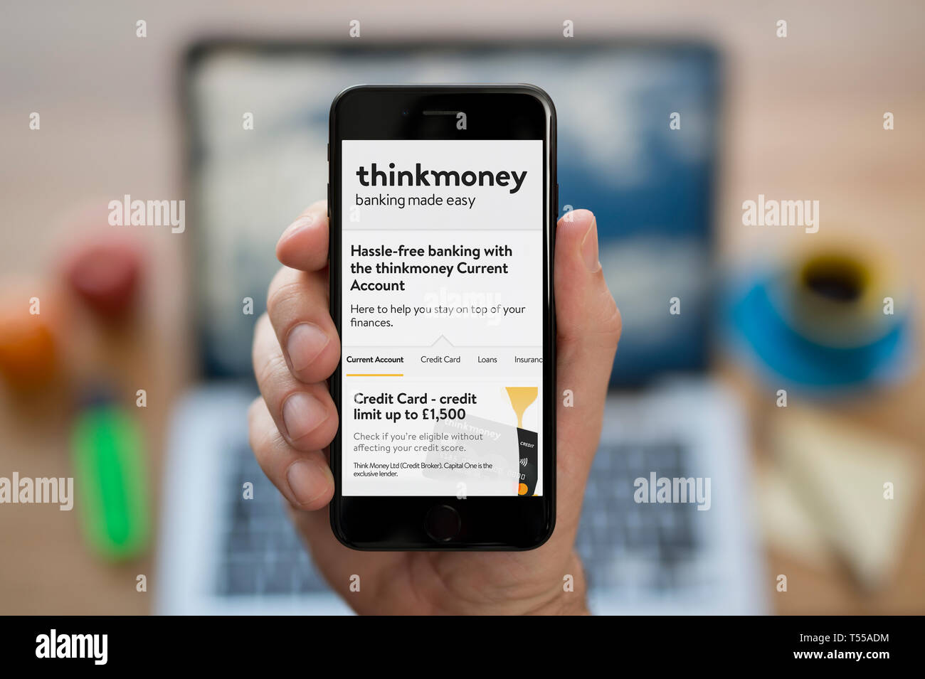A man looks at his iPhone which displays the Thinkmoney logo (Editorial ...