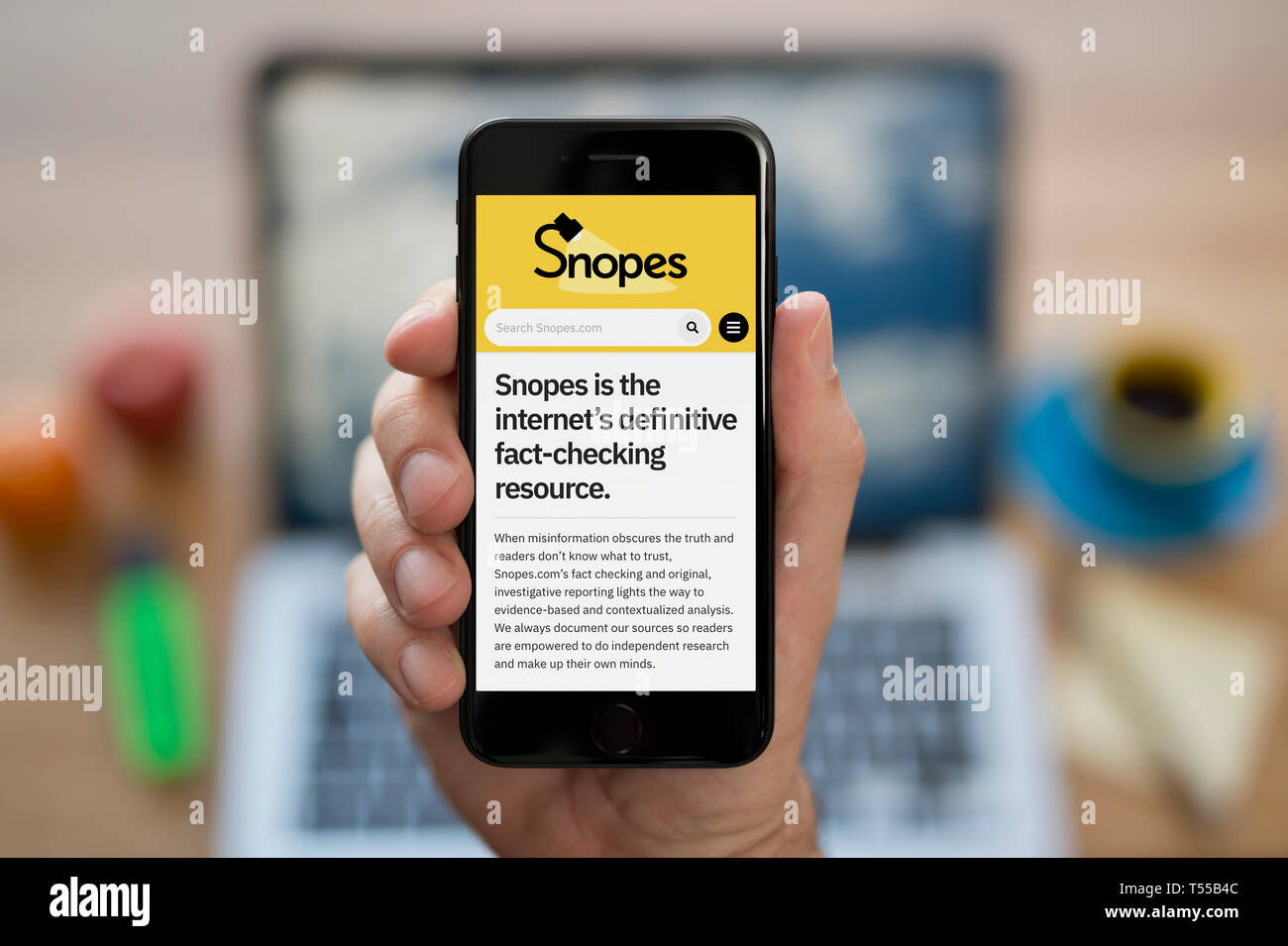 A man looks at his iPhone which displays the Snopes logo (Editorial use ...