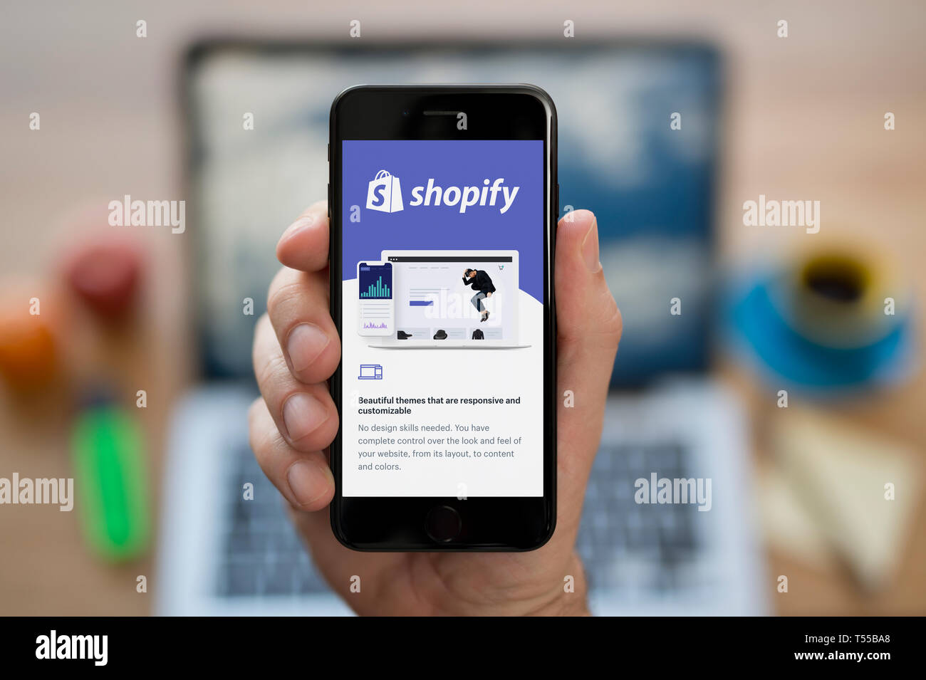 A man looks at his iPhone which displays the Shopify logo (Editorial ...