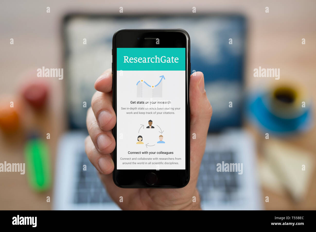 A man looks at his iPhone which displays the Research Gate logo ...