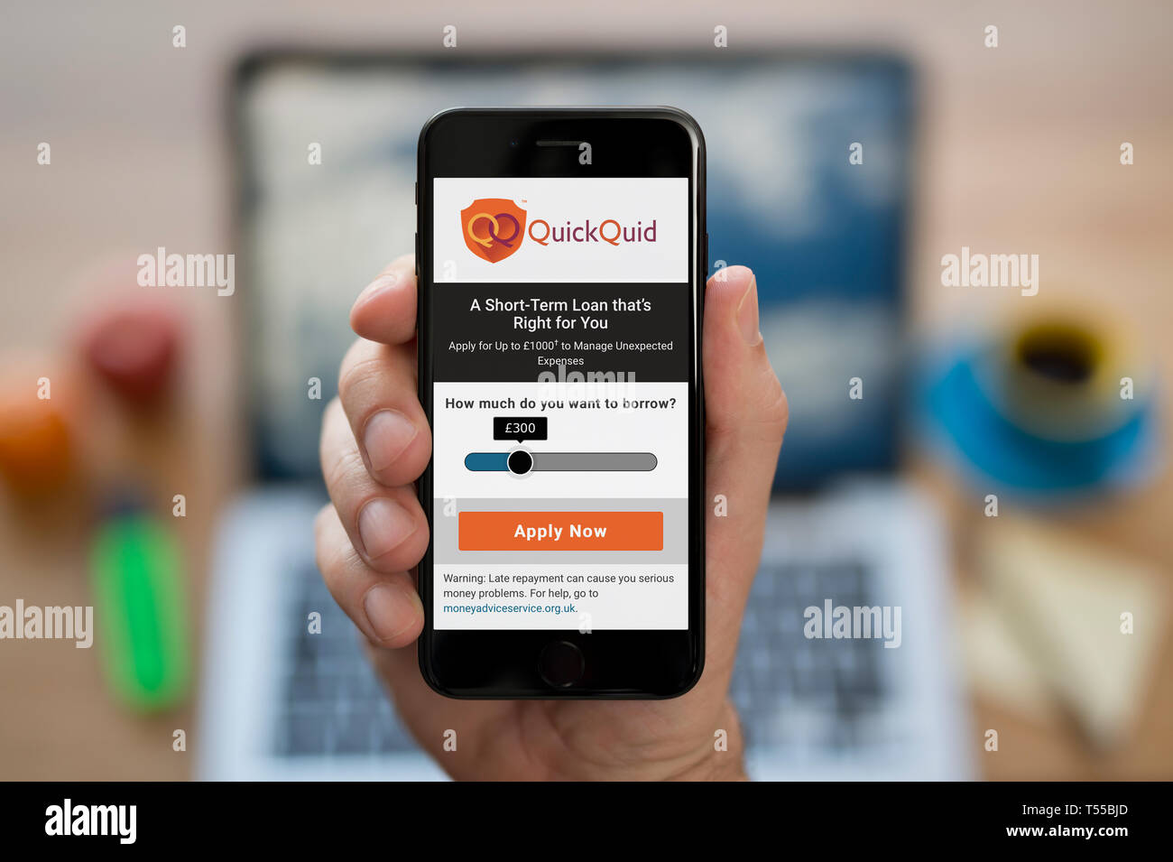 A man looks at his iPhone which displays the Quick Quid logo (Editorial ...