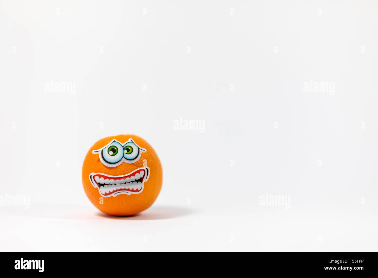 Whole orange with an apprehensive cartoon like face set on a white ...