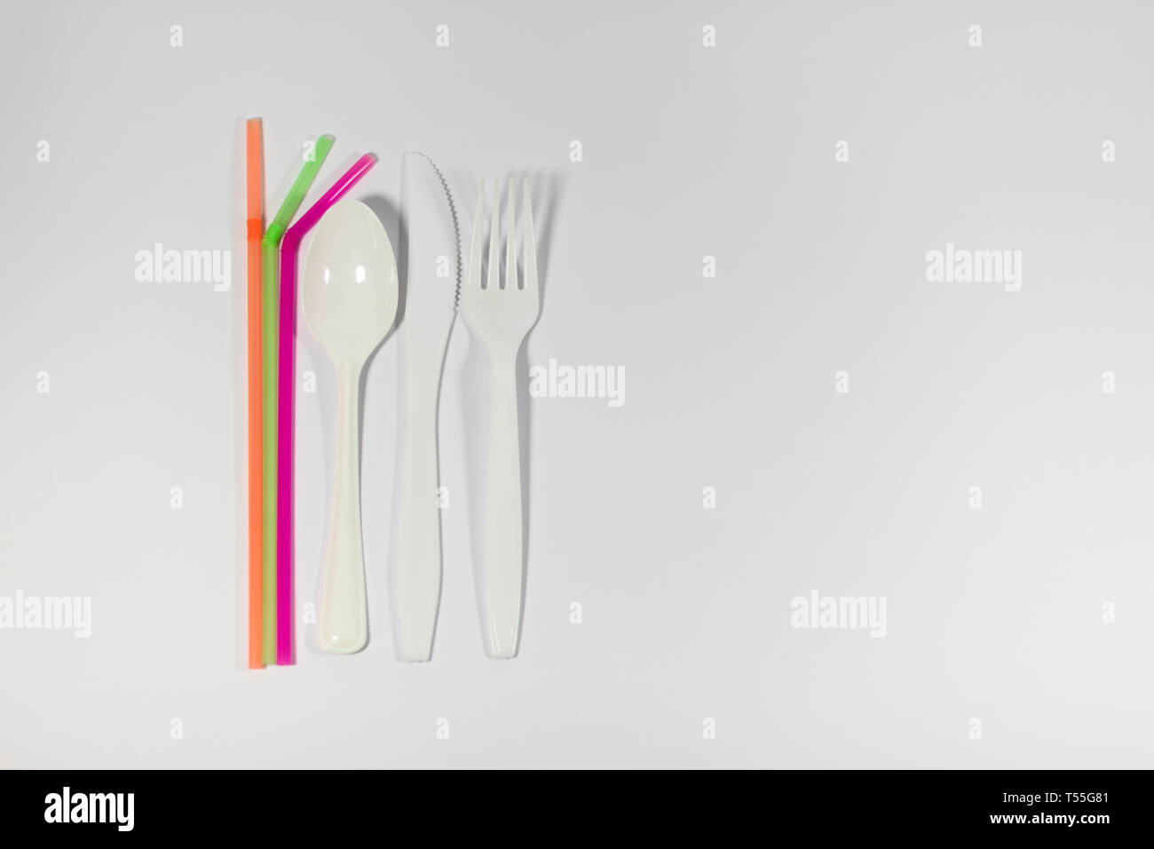 Plastic single use utensils and plastic single use straws, set on a ...