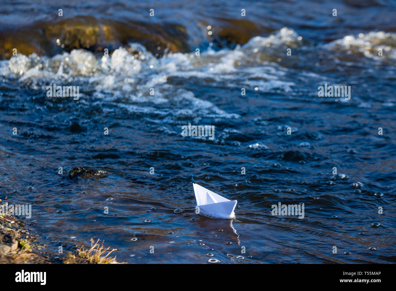 A paper boat on a turbulent stream of water struggles with the flow ...