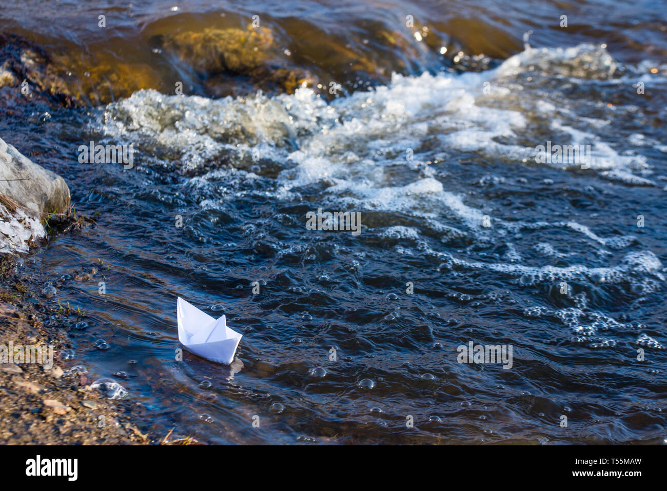 A paper boat on a turbulent stream of water struggles with the flow ...