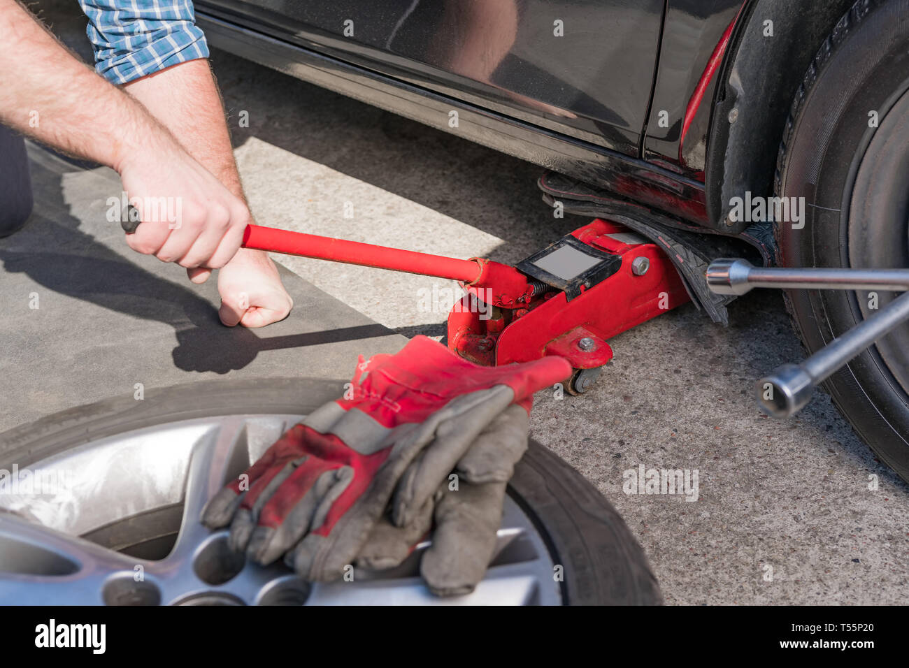 Man jacking up car on a driveway. Seasonal tyre change or service ...