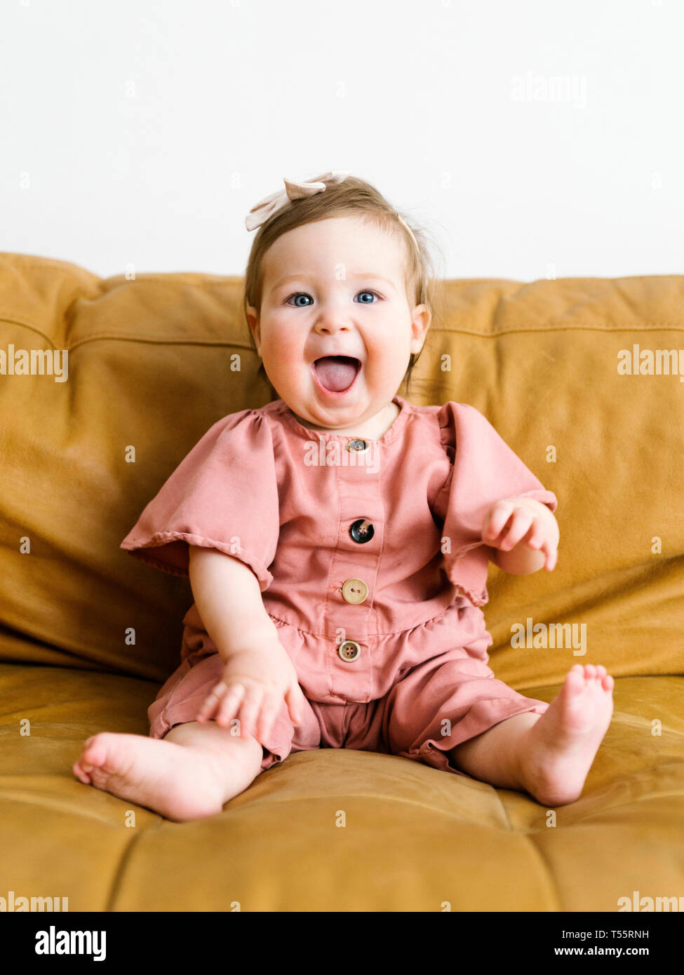 Baby girl wearing pink outfit on sofa Stock Photo - Alamy