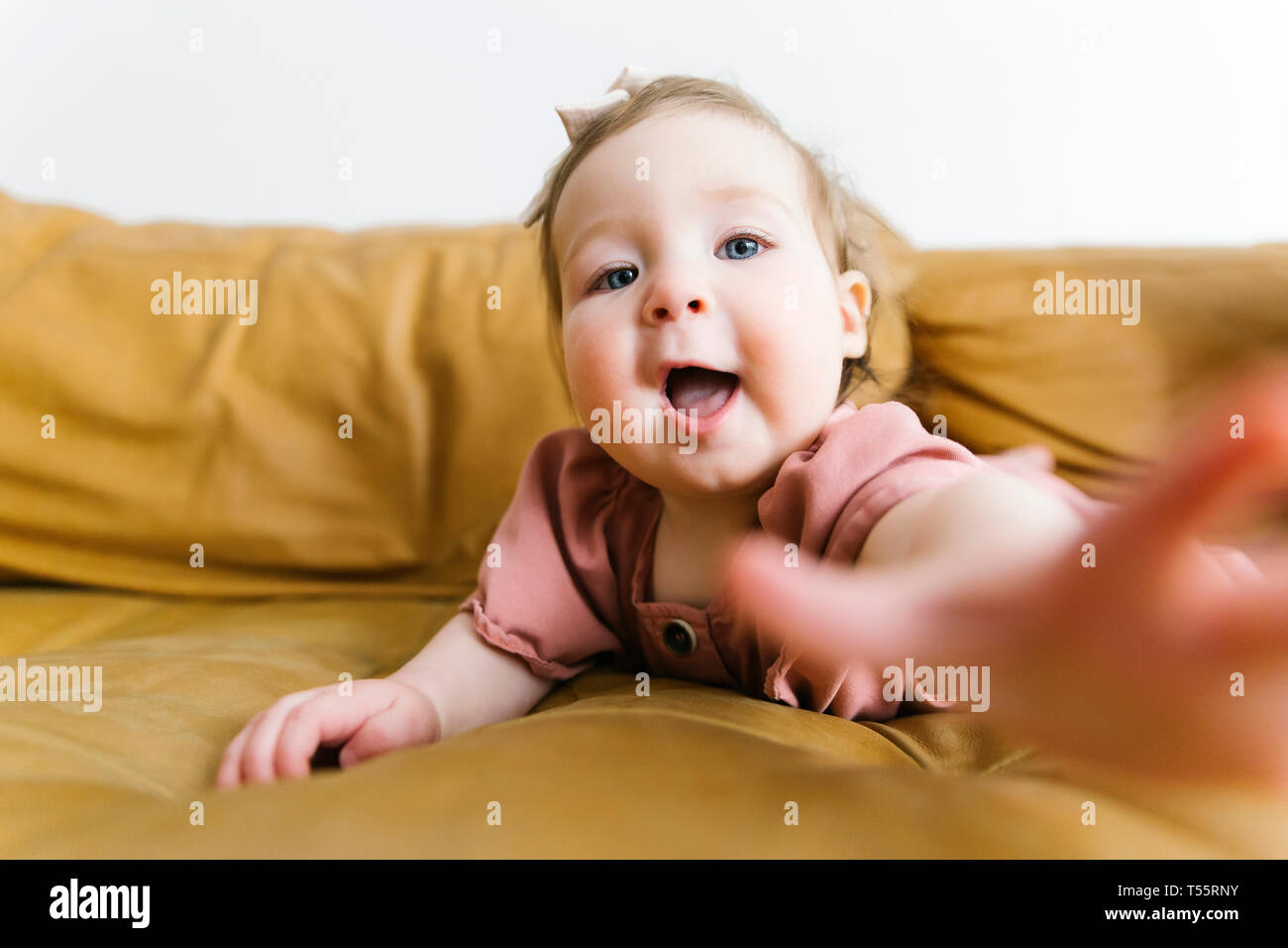 Baby girl reaching for camera on sofa Stock Photo - Alamy