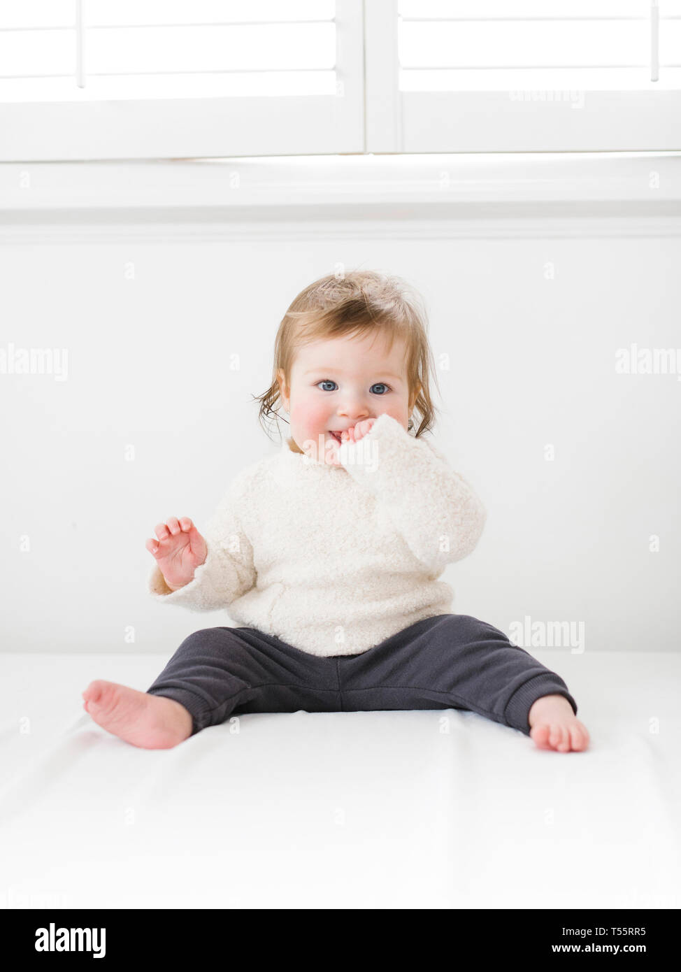 Baby girl sitting under window Stock Photo - Alamy