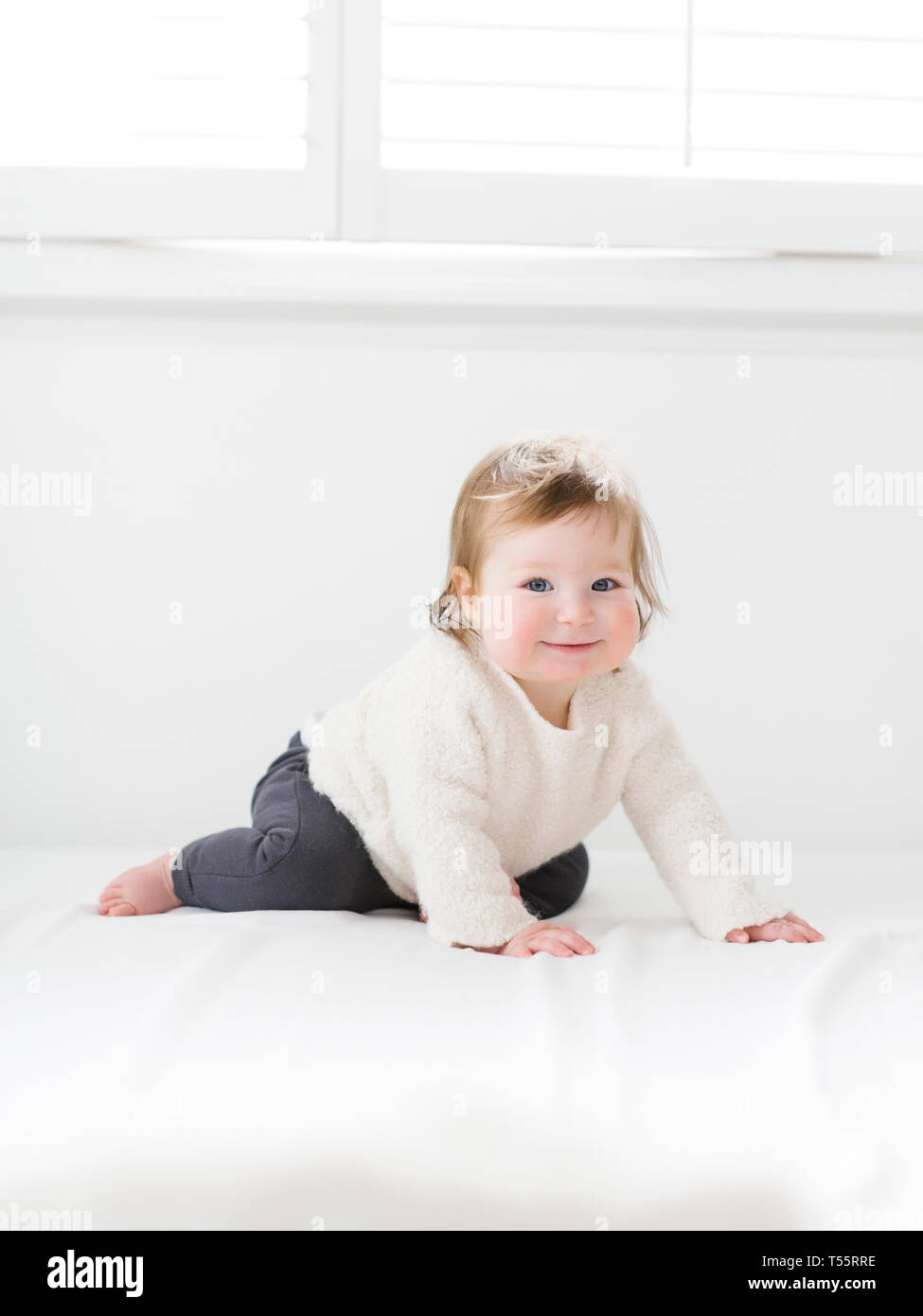 Kneeling baby girl under window Stock Photo - Alamy