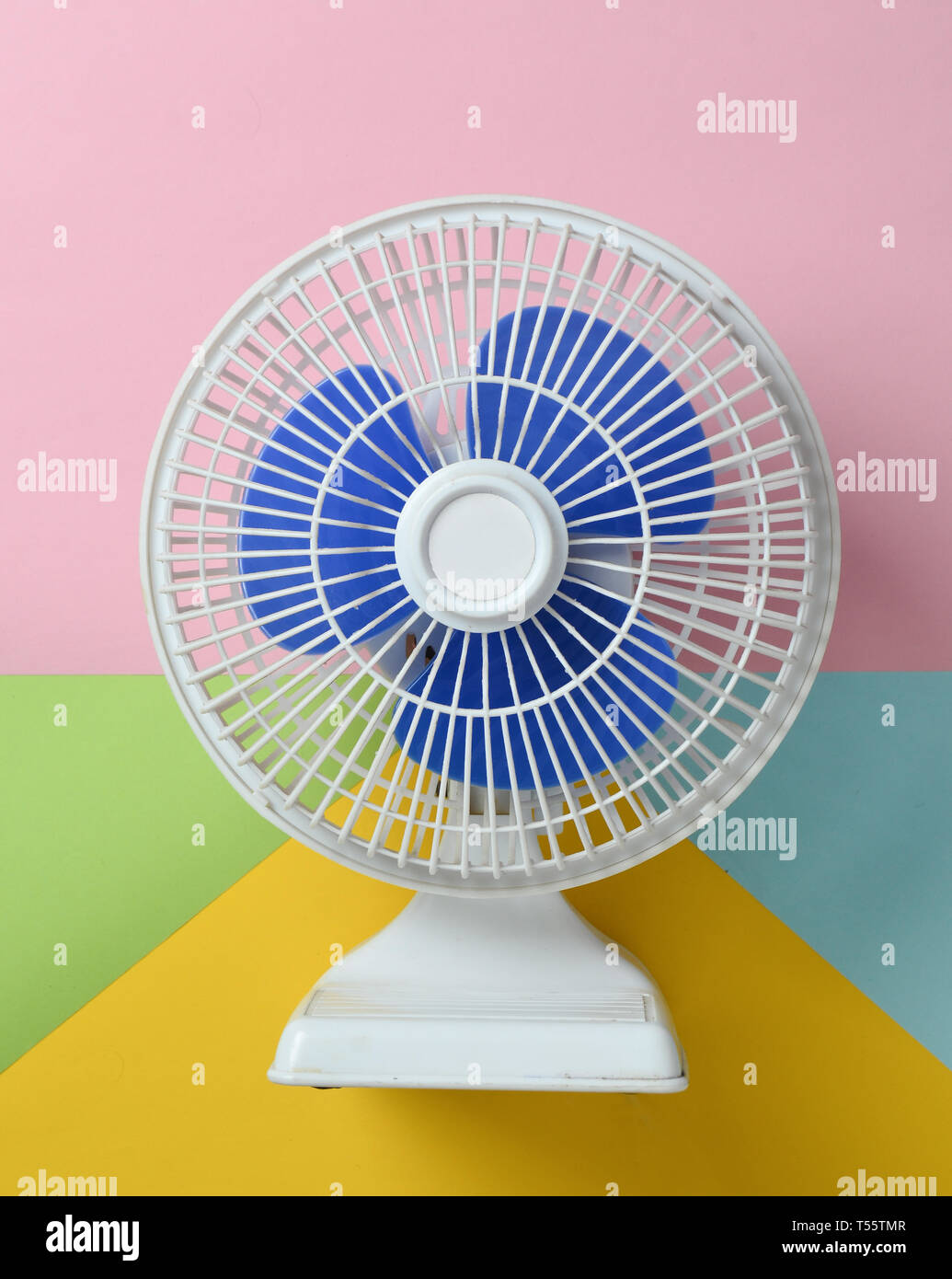 White plastic fan with blue louvres on a multicolored pastel background ...