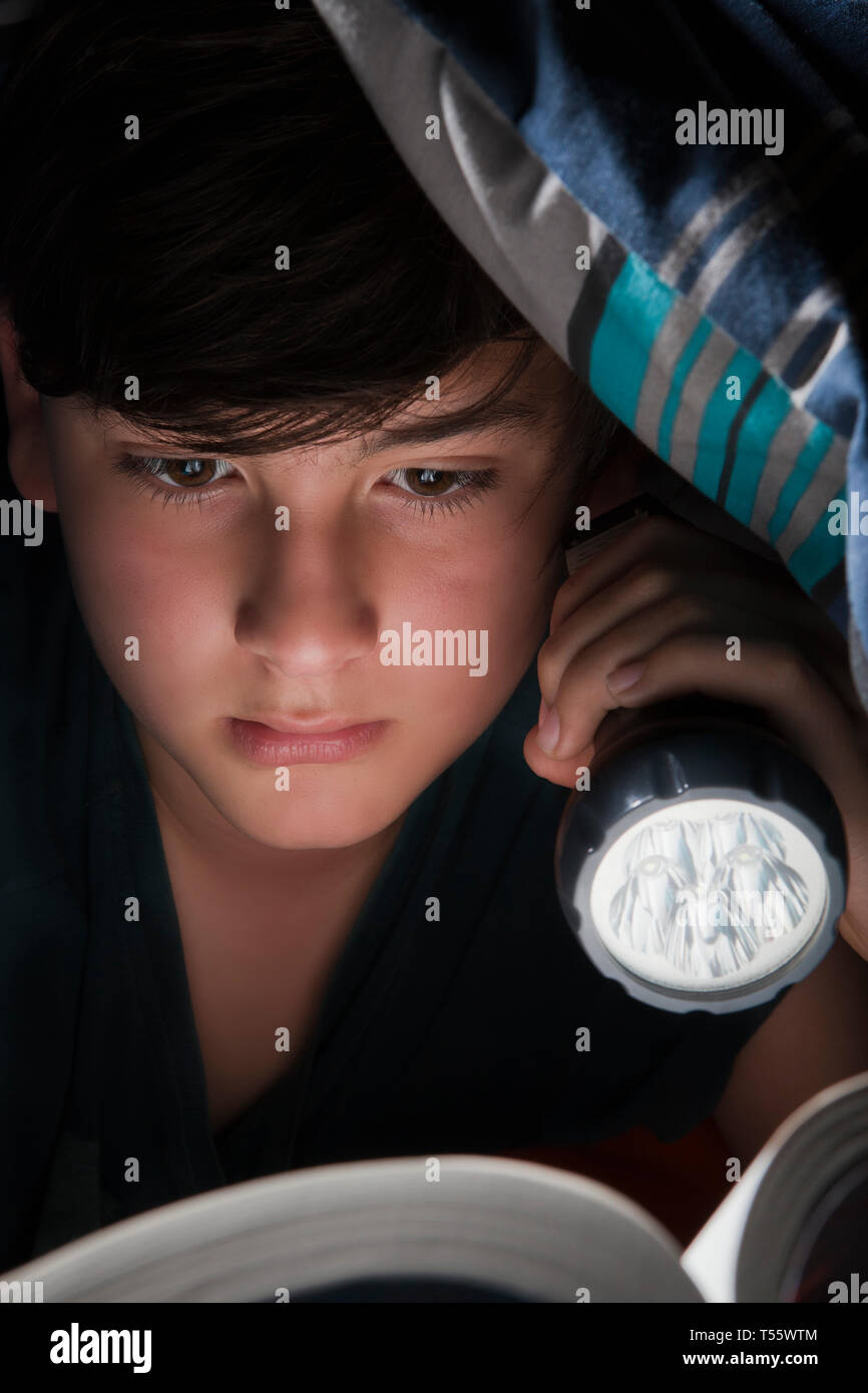 Boy reading with torch under blanket Stock Photo - Alamy