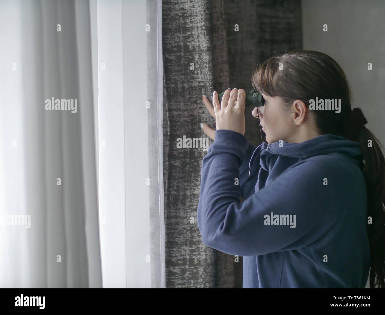 Woman watching through binoculars through the window Stock Photo - Alamy