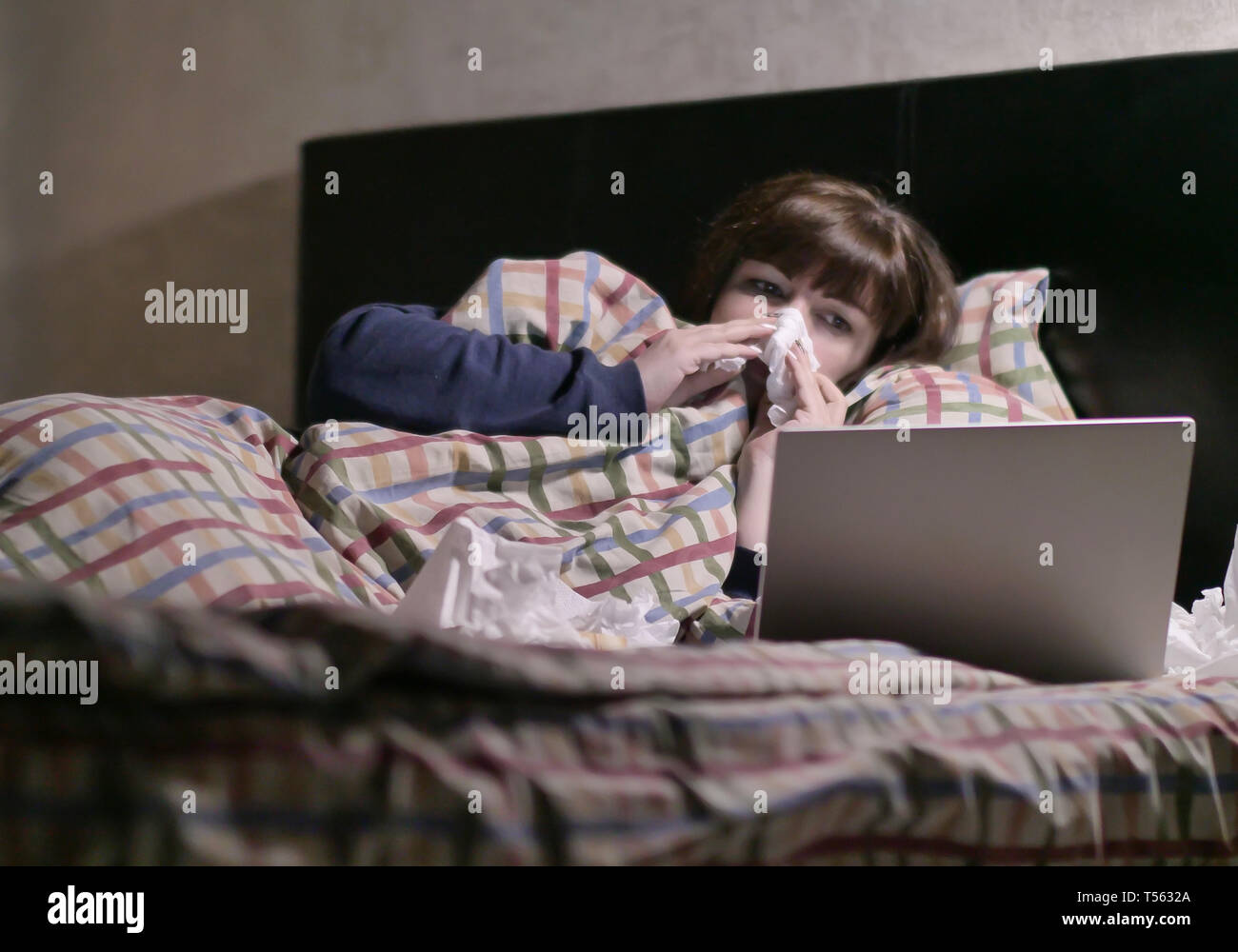 Sick pretty girl is lying in the evening in bed and watching a laptop ...