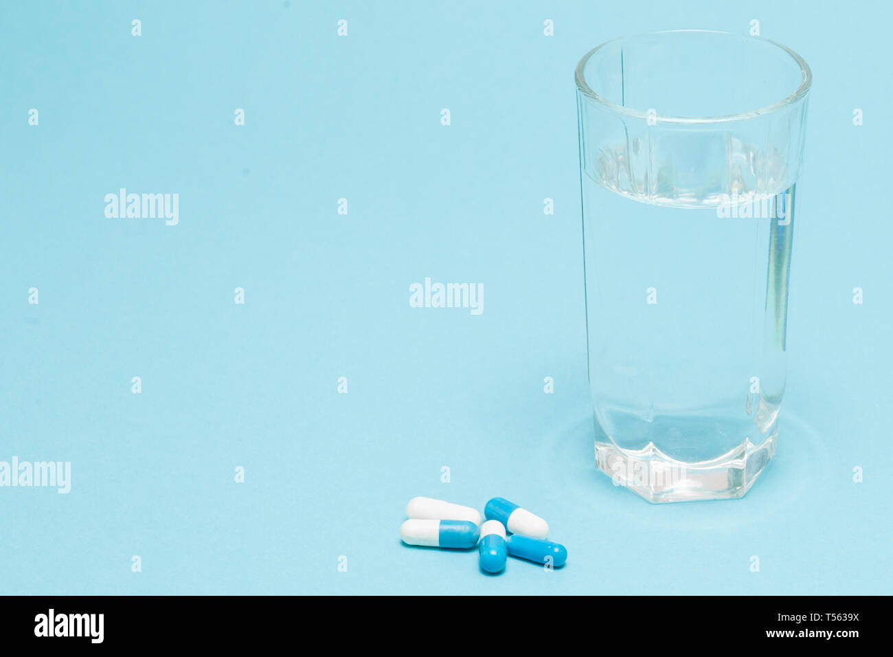Swallowing tablets. Pills and a glass of water against a blue table ...