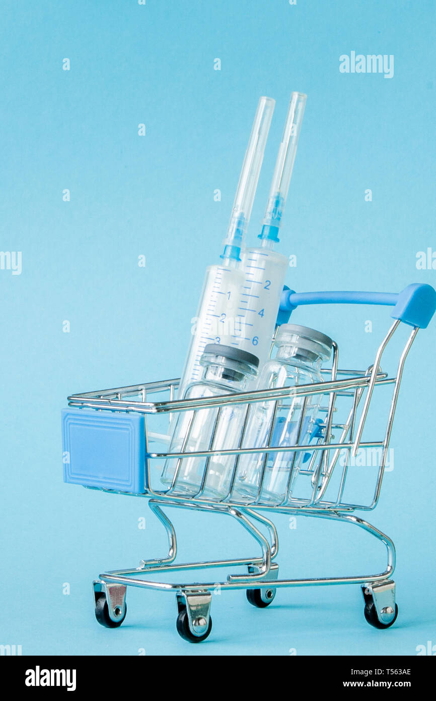 Medical injection in shopping trolley on blue background. Creative idea ...
