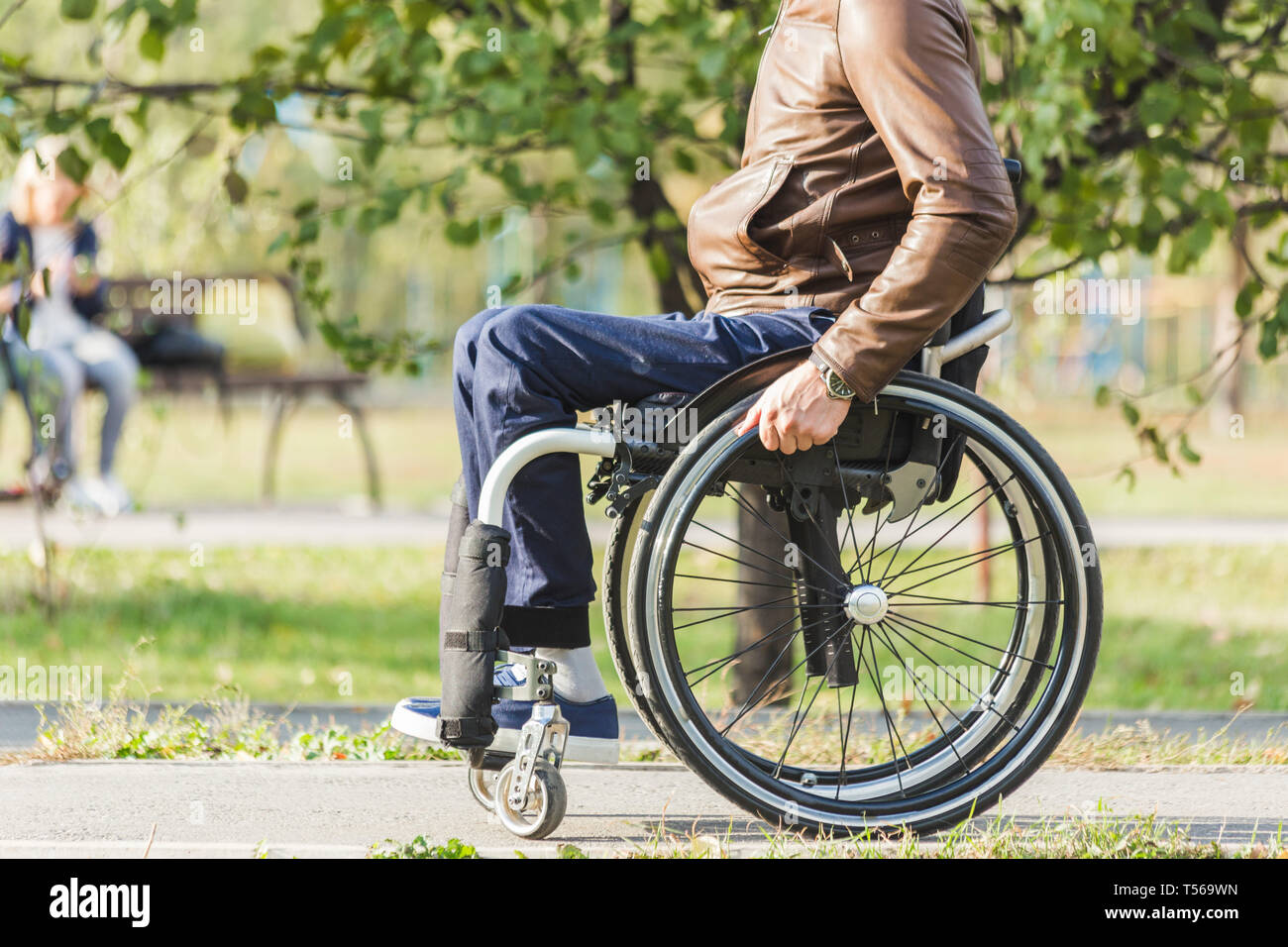 A young man in a wheelchair rides along the park road Stock Photo - Alamy