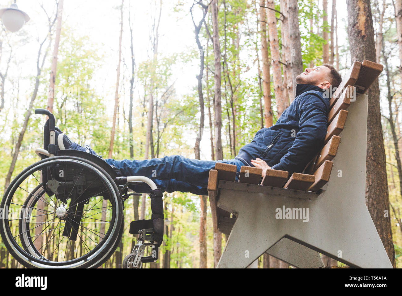 Young man resting sitting on a bench with his legs on his wheelchair ...