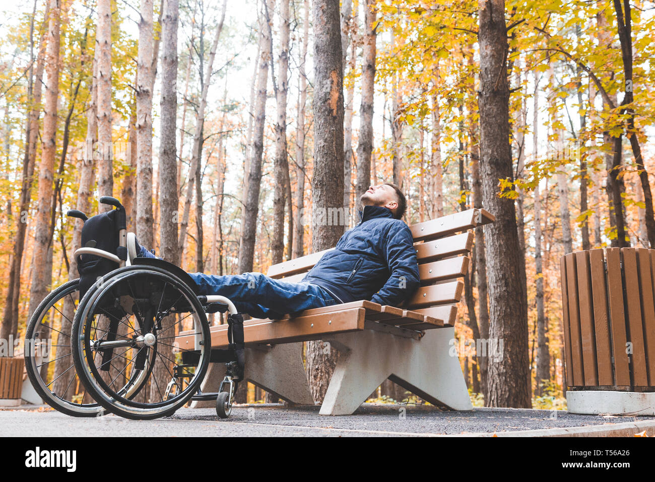 Young man resting sitting on a bench with his legs on his wheelchair ...
