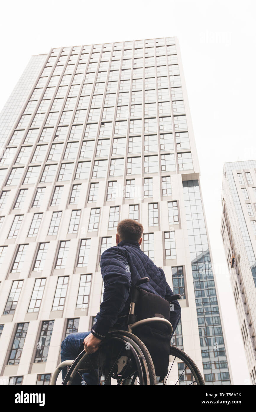 Young man in a wheelchair against the backdrop of a modern high-rise ...