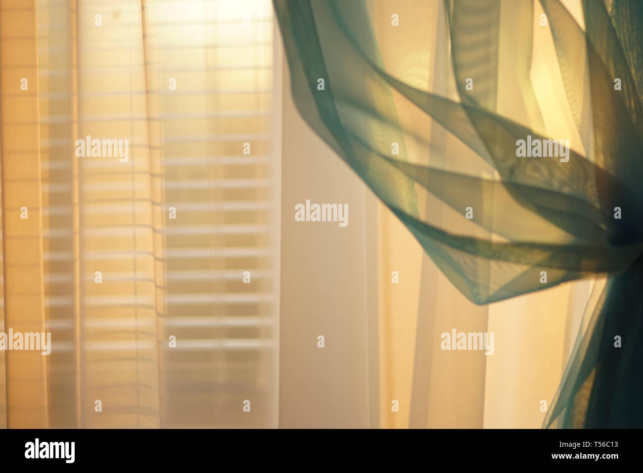 Sunny sunset light through the thin curtains on the window with blinds ...