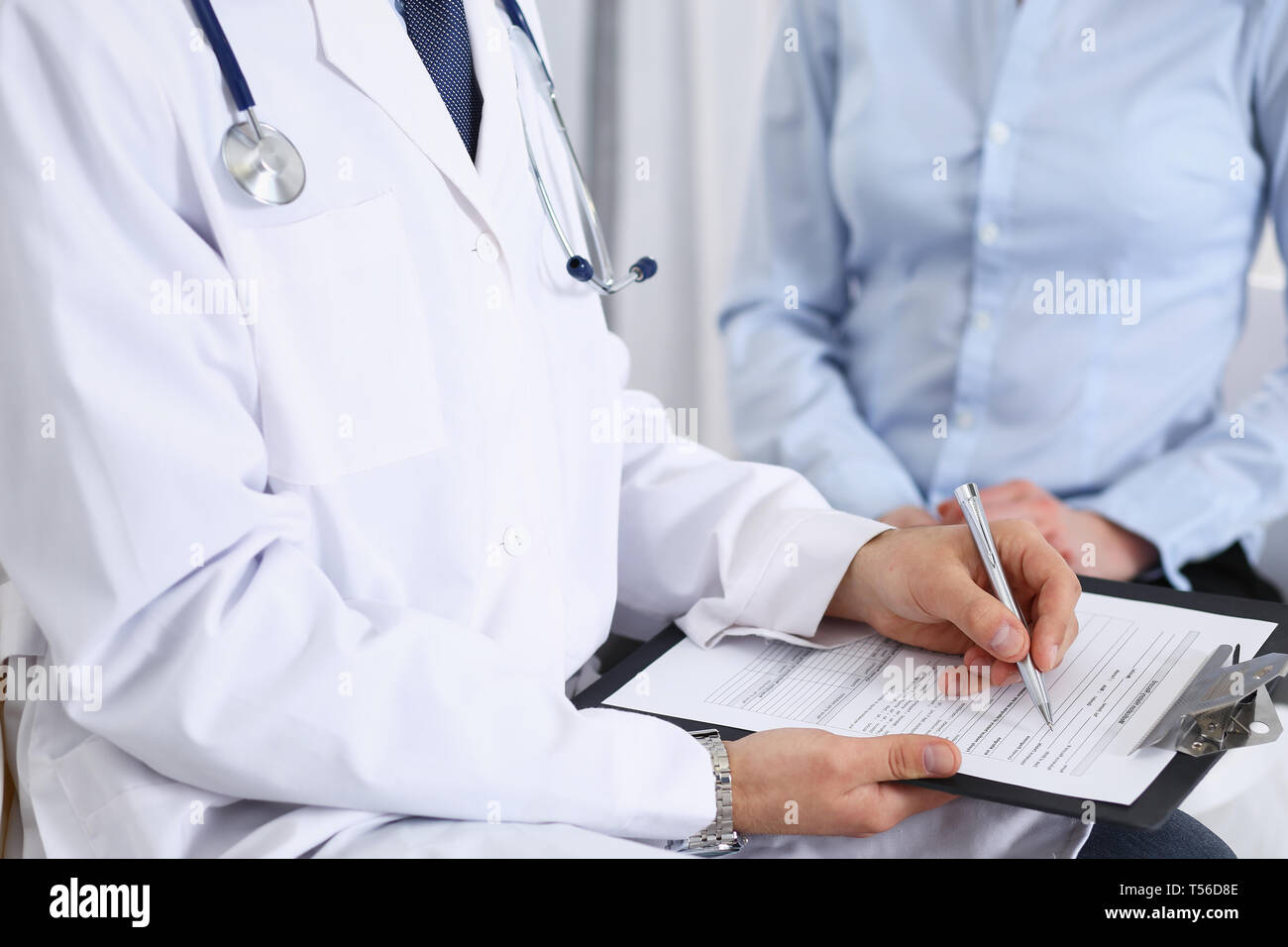 Male doctor holding application form while consulting female patient in ...
