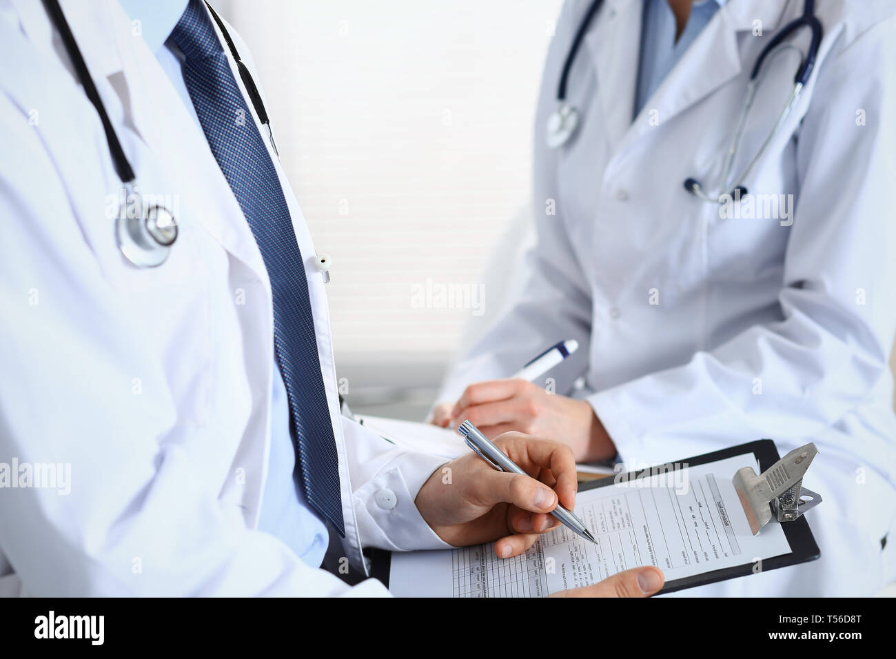 Two unknown doctors filling up medical form on clipboard, just hands ...