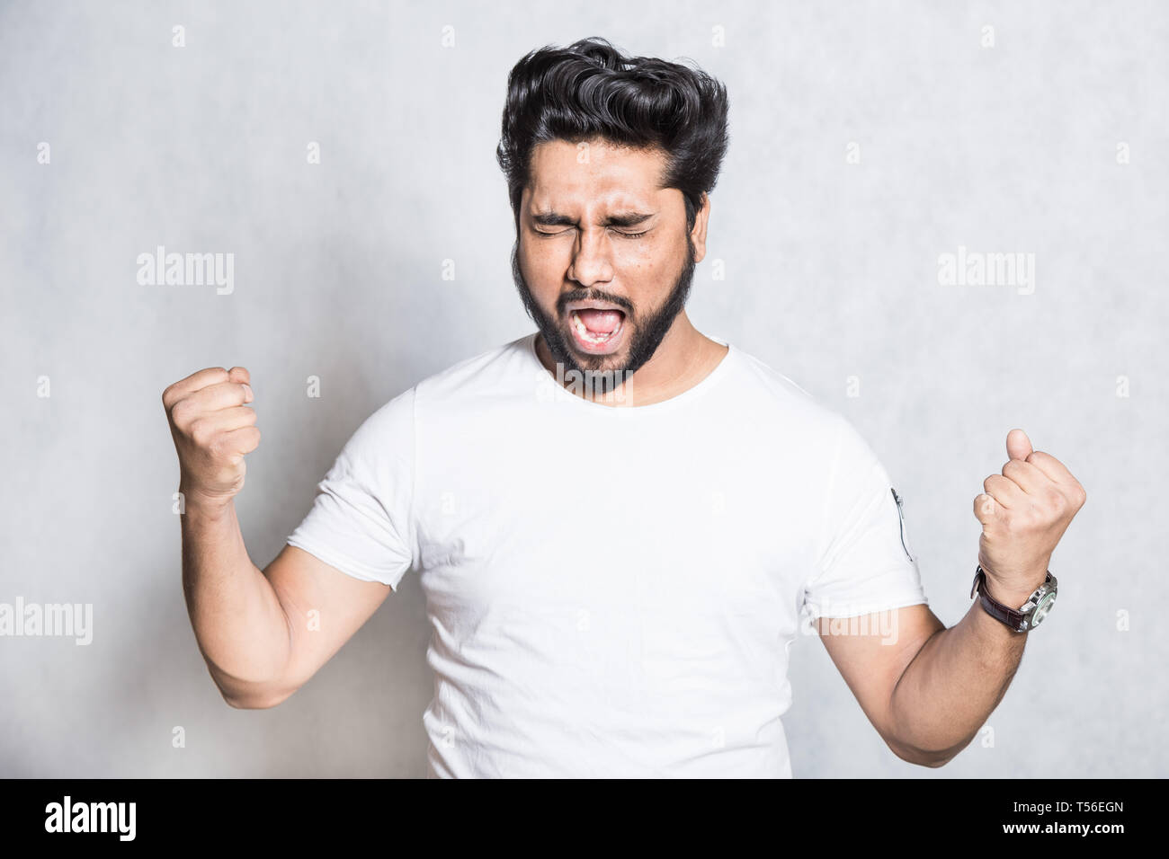 Portrait of overjoyed man clenches fists with happiness, poses against ...